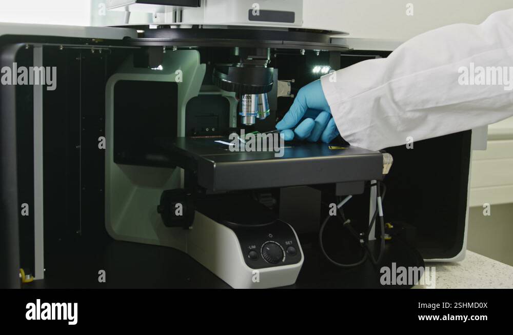 A slide is placed under the lens of a big microscope, which closes up ...