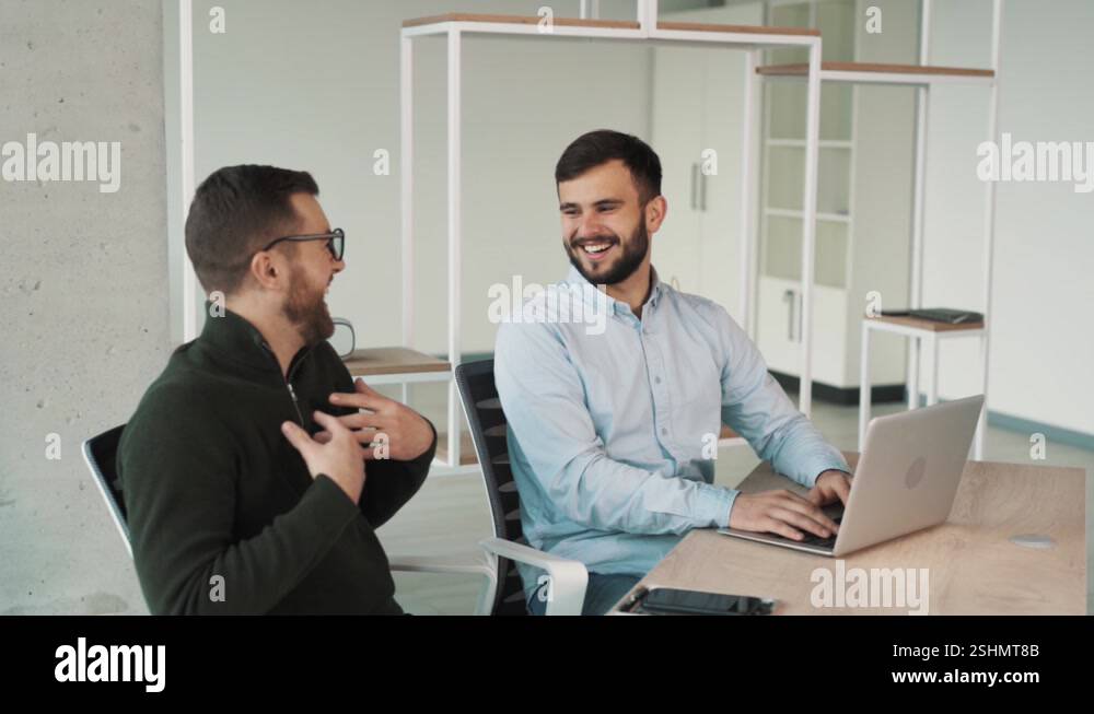 A solid man tells a funny joke to a colleague around the office, and ...