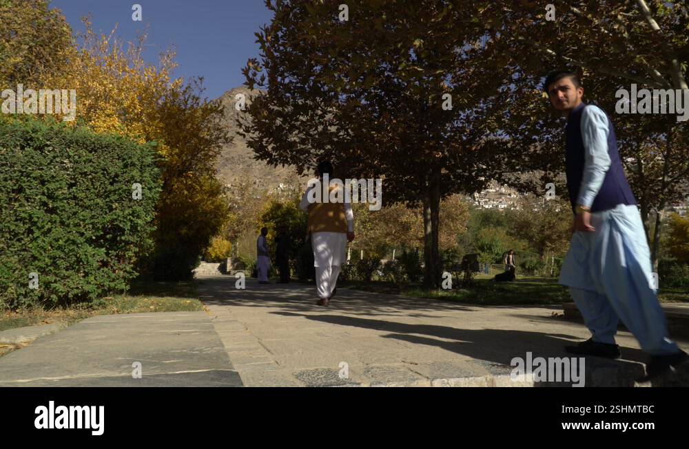 Afghan men and boys in traditional clothes walk in park, static view ...