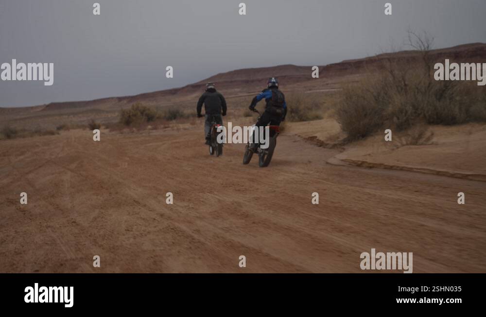 Tracking shot behind dirt bikers in red sandy wash in Utah desert ...