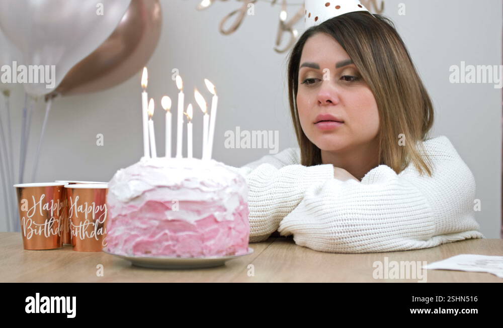 Sad birthday. Beautiful girl sits alone in front of a birthday cake and ...