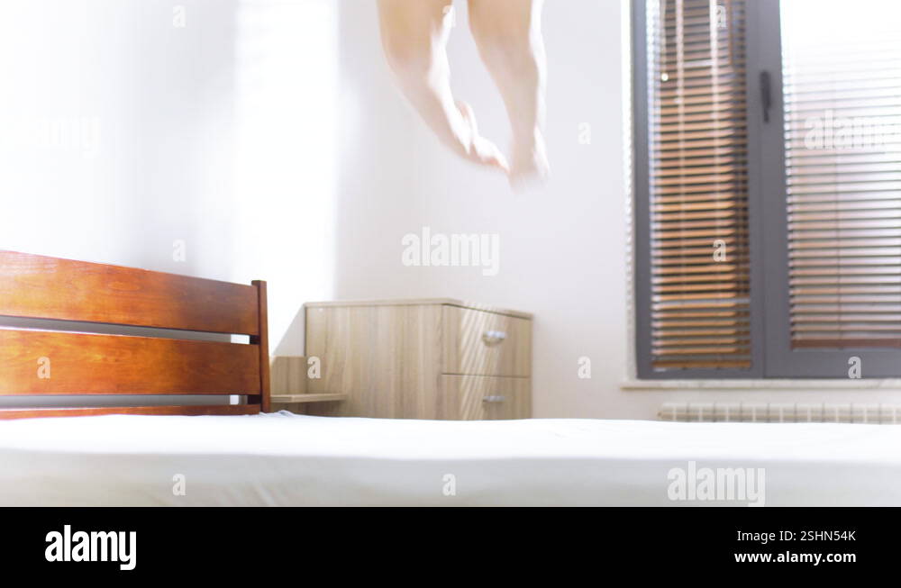 Beautiful happy young woman jumping on a bed at home. Girl in silk robe ...