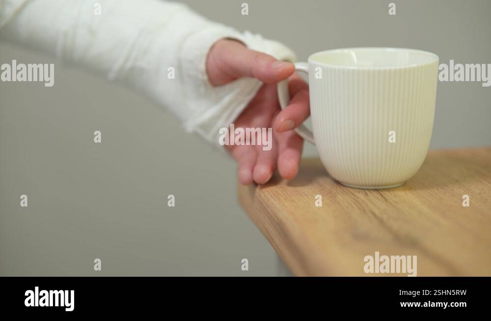 A man with a broken arm in a plaster cast takes and puts a mug of the ...