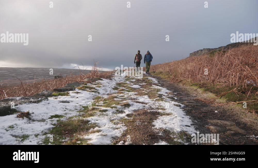 Two men hiking down a snowy, countryside trail towards the camera in ...