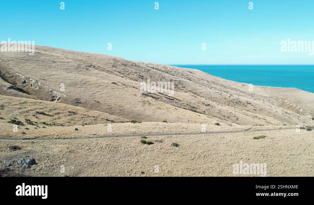 Flying sideways parallel to gravel road as barren peninsula hills drop ...