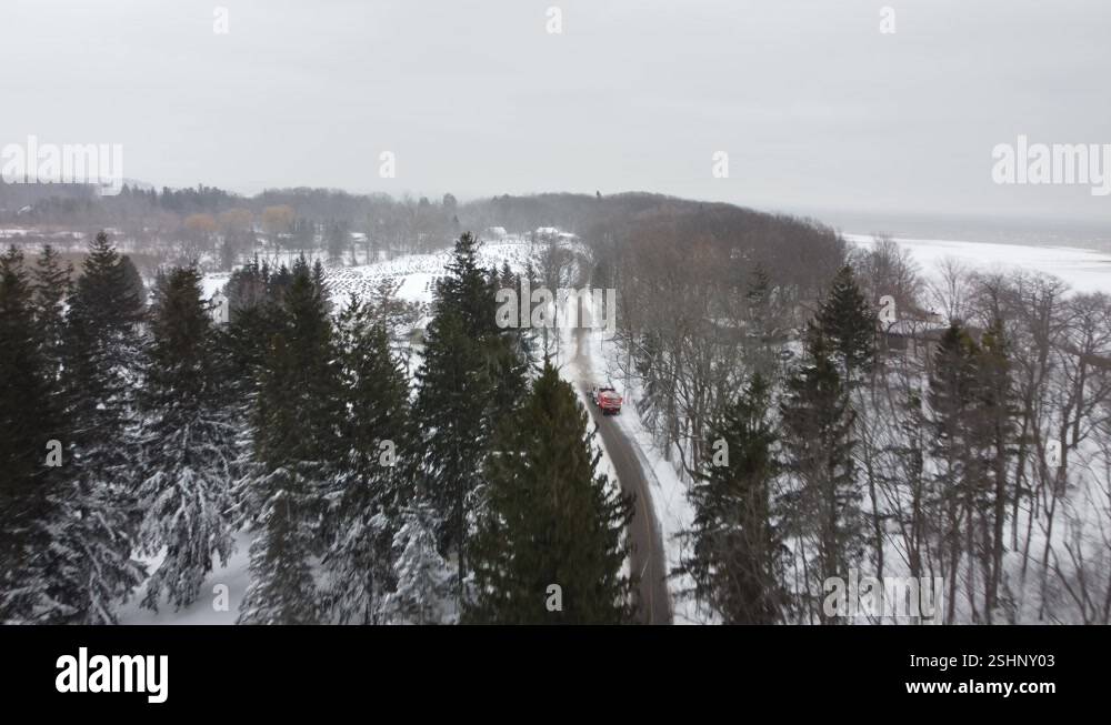 A road plow clears the road of snow on a path leading between a forest ...