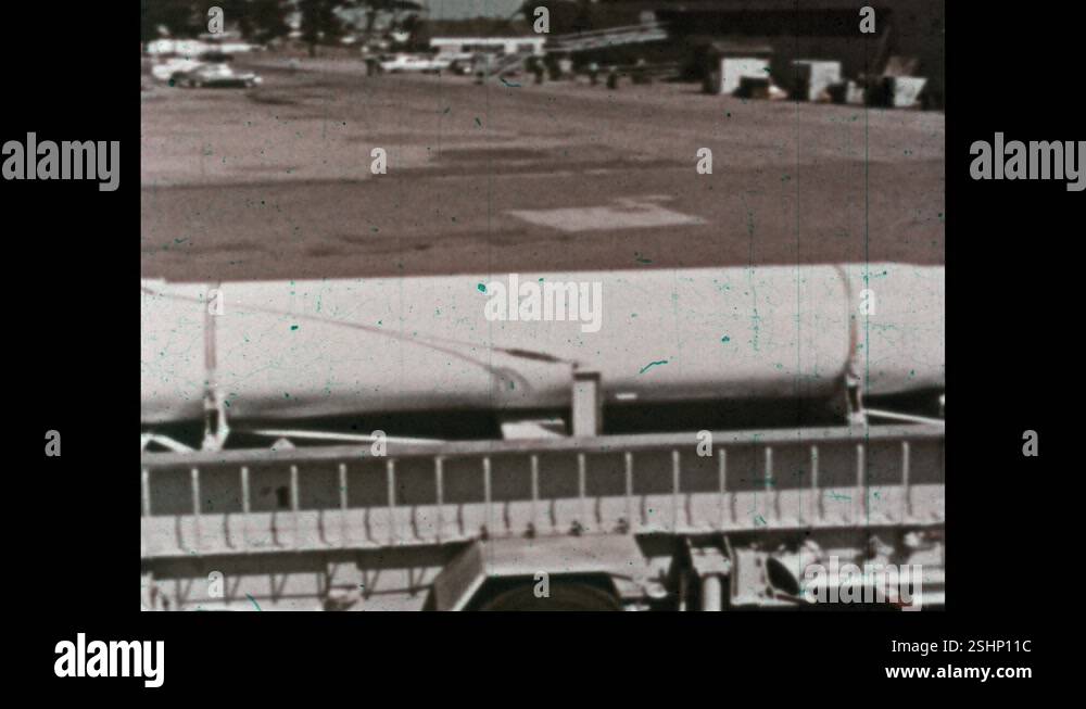 1950s: Truck pulls flatbed trailer with rocket. Trailer and rocket are ...