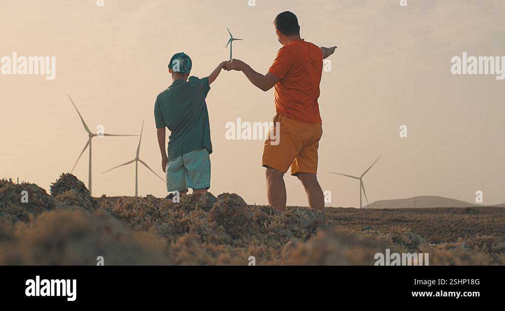 Happy father and son on looking at wind energy turbine sat wind farm ...