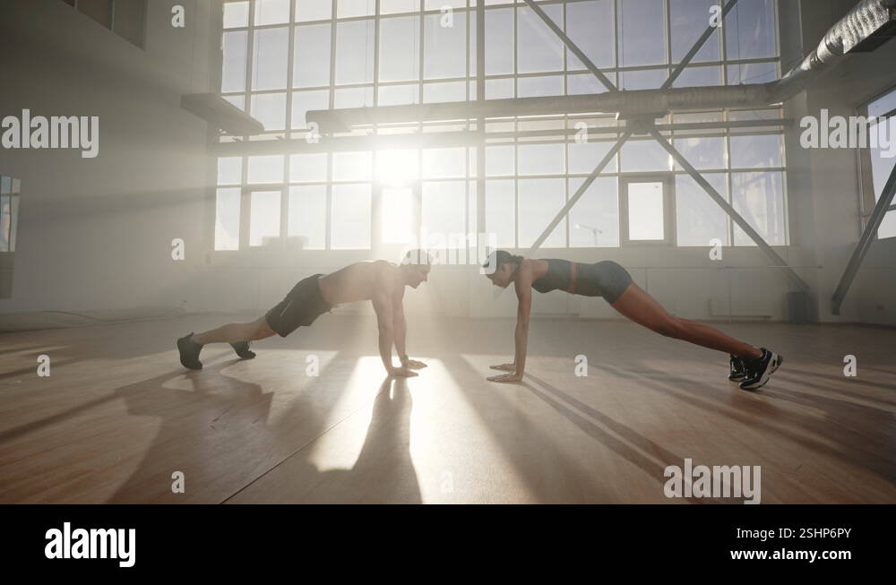 Young multi-ethnic couple of sports people training in sync in the gym ...