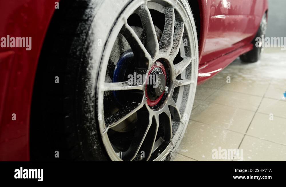 Man washes a red Subaru at a car wash. Close-up of car wheels with OZ ...