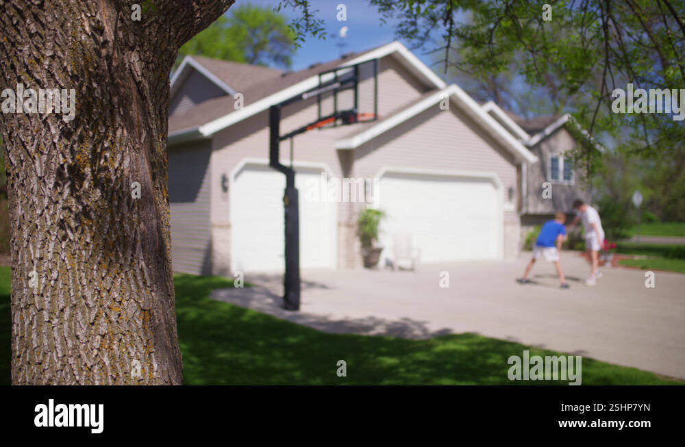 Two Teenage Boys Playing Playing Basketball In Their Driveway On a Blue ...