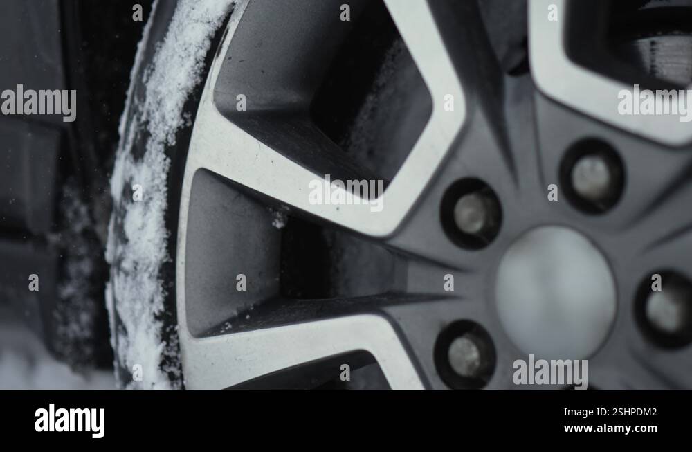Grey car big wheels slowly spin and spit up heavy wet snow as unknown ...