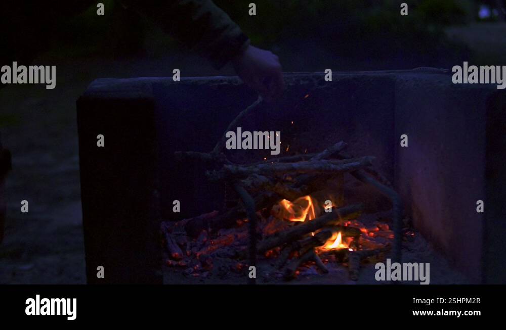 Close-up of a person throwing sticks of wood into a bonfire in a stone ...