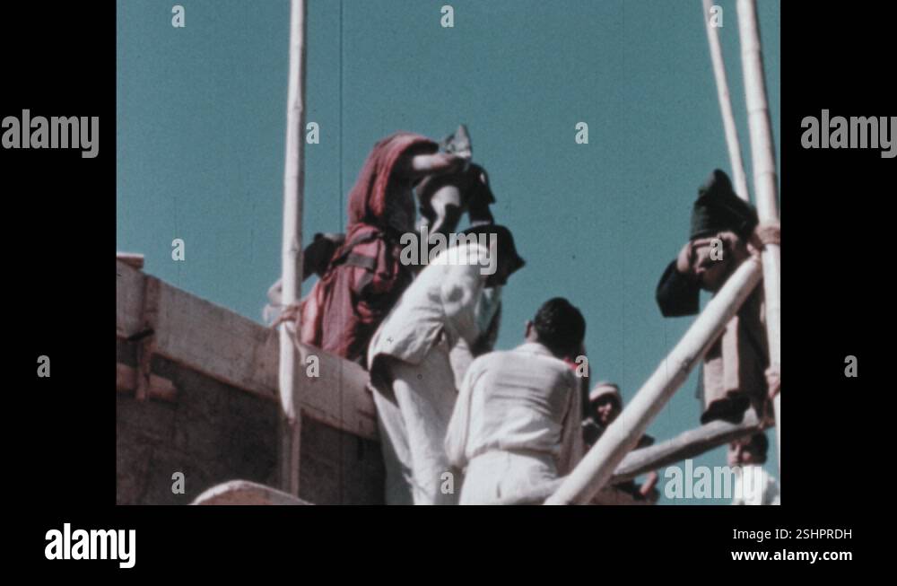 1950s: Tilt up, chain of people lifting bowls onto roof. Man outside ...