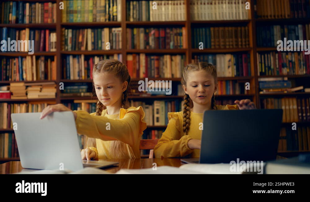 Two sisters identical twins using laptops to study in school library, teamwork Stock Video ...