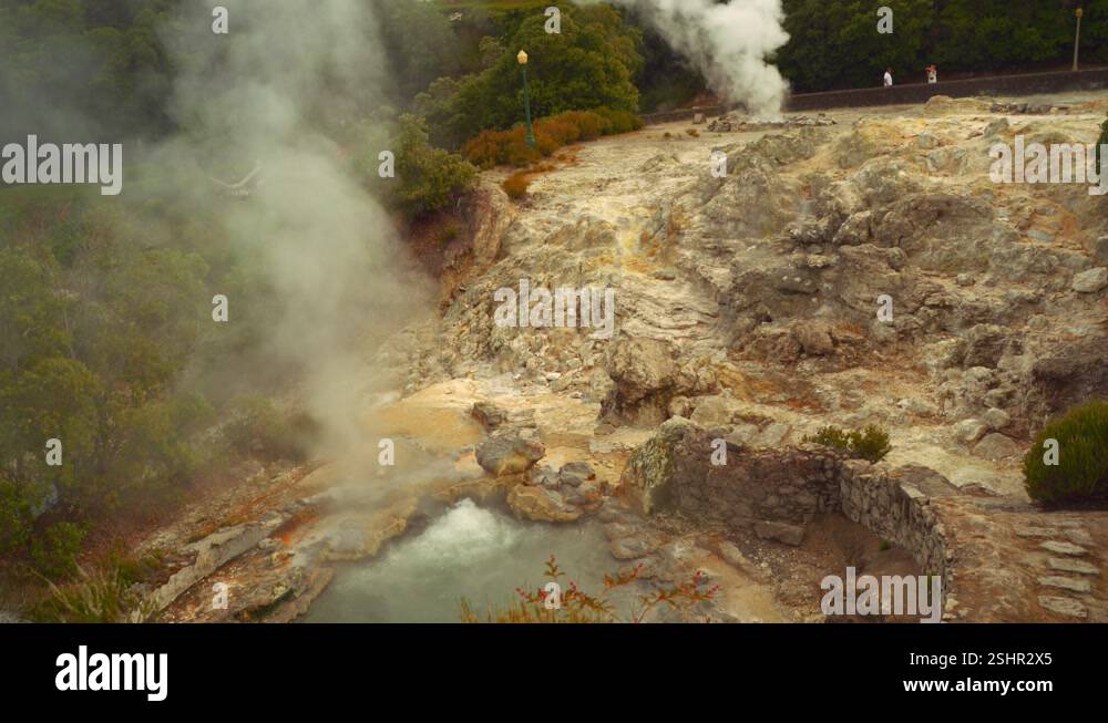 A scenic pan with a view of two geothermal pools that emit steam from ...