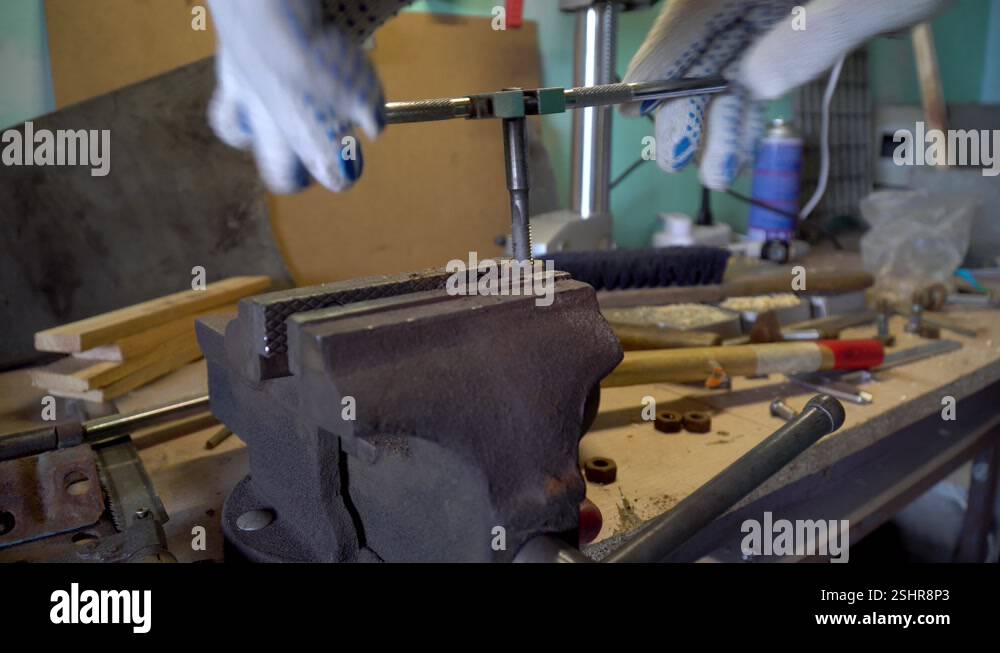 Close up worker cuts the damaged thread of a nut bolt clamped in a vise ...