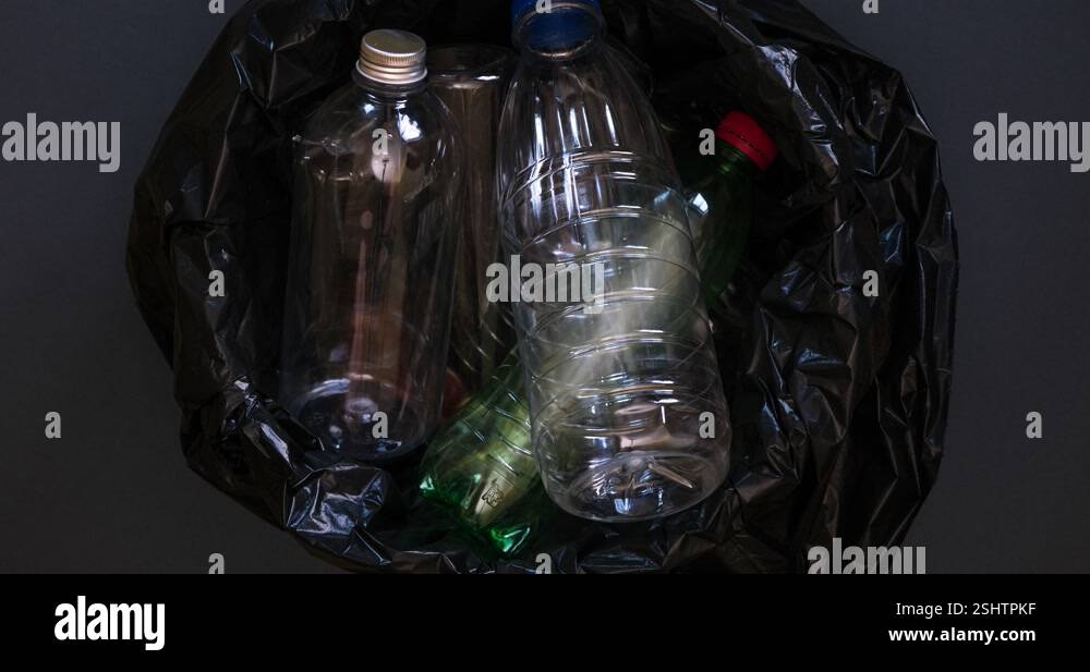 Empty plastic bottles fall into the trash can with a black plastic bag ...