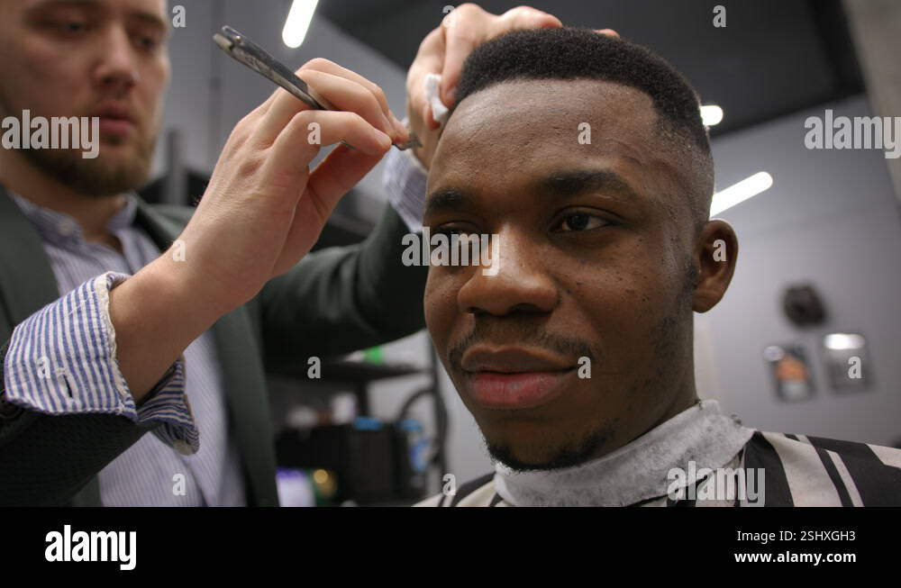 Barber shaving aligning curly hair afroamerican man using razor in ...
