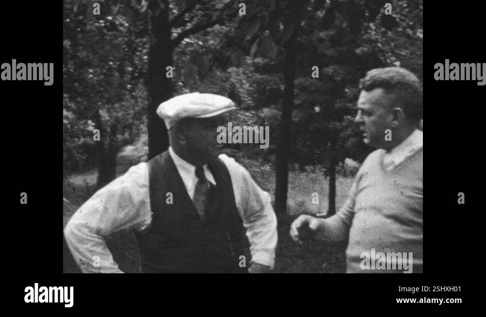 1930s: Group of men stand around talking in a wooded area. Leader ...