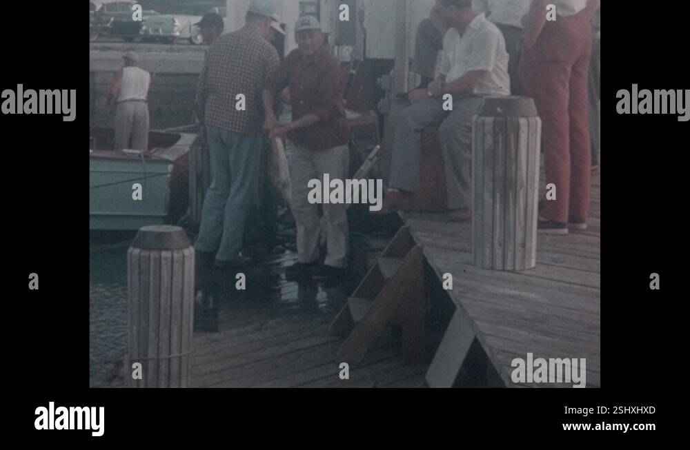 1950s: Men show catch on a dock. Older man picks up a smaller fish and ...