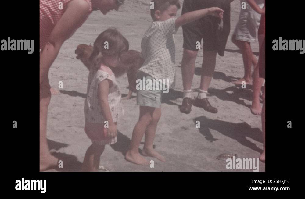 1950s: Fish flop on the beach. People stand around the fish, little boy ...