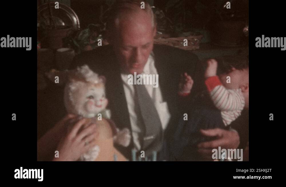 1950s: Man sits at table and holds baby in lap. Baby starts crying ...
