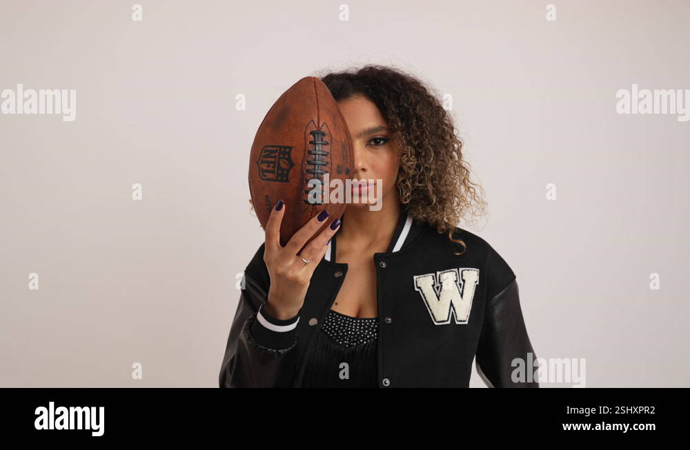 curly-haired cheerleader holding an American football near to her face ...