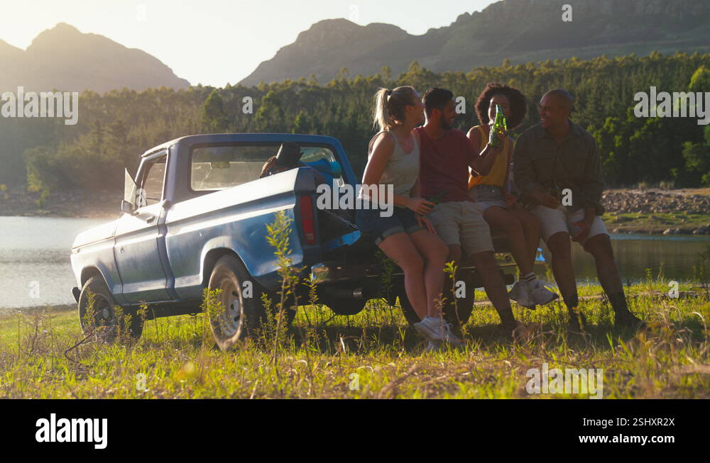 Friends With Backpacks Sitting On Tailgate Of Pick Up Truck On Road ...