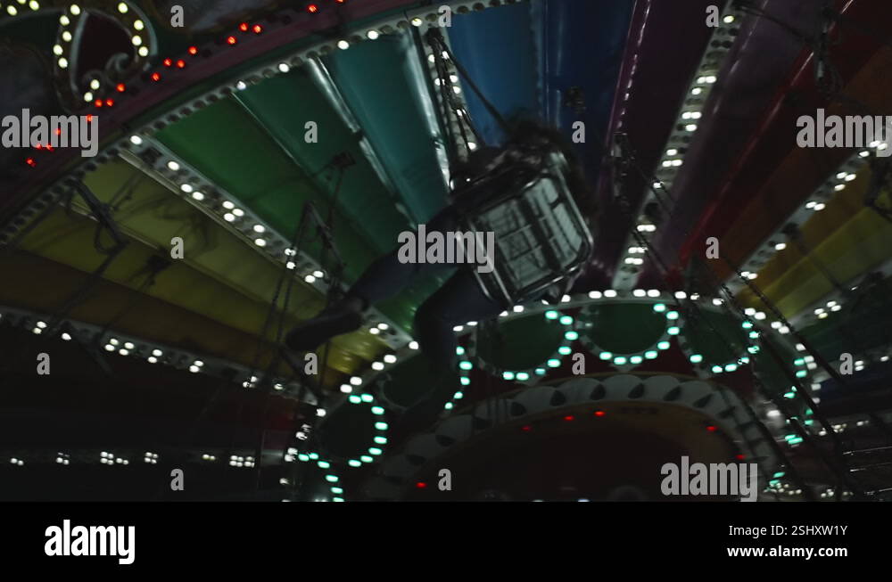A young woman rides alone late at night on a carousel. Mountains behind ...
