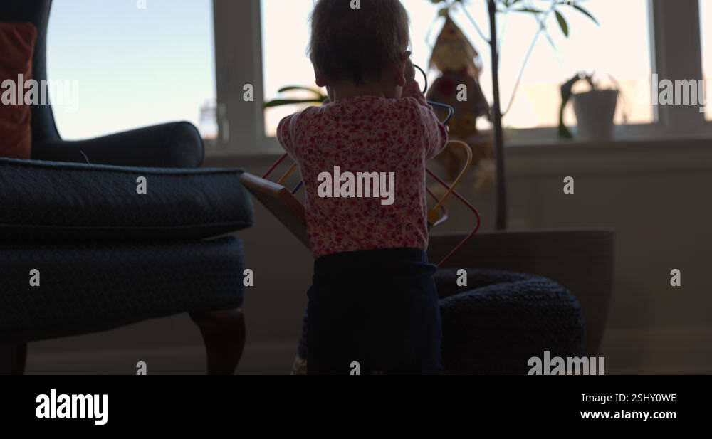 Toddler girl walks around living room with her puzzle toy - from behind ...