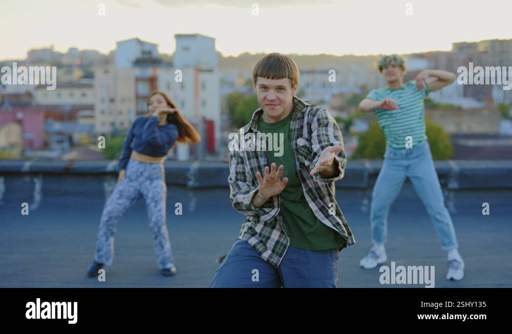 Three people dancing on the roof looking at camera. Young man dancing ...