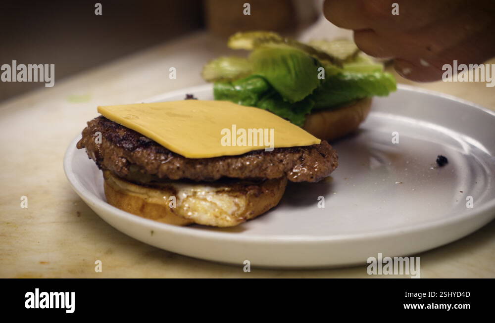Messy chef builds cheeseburger dropping cheese slice in background and ...