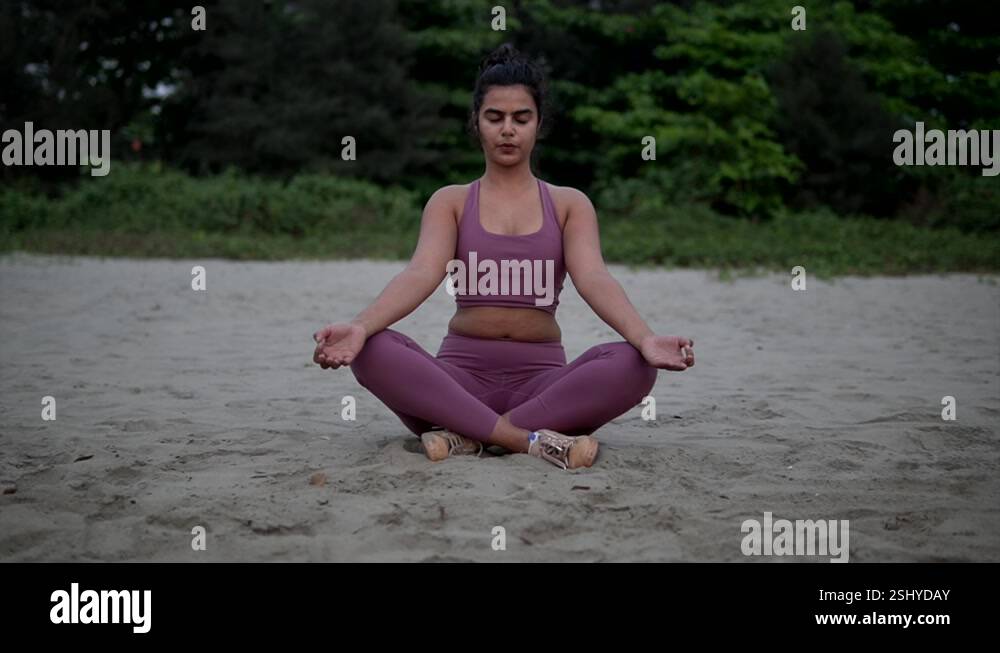A fit young woman while practicing a yoga easy pose, Sukhasana, on an ...