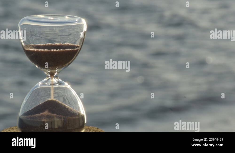Sand Timer in a blue beach at sunset. Time is running out, climate ...