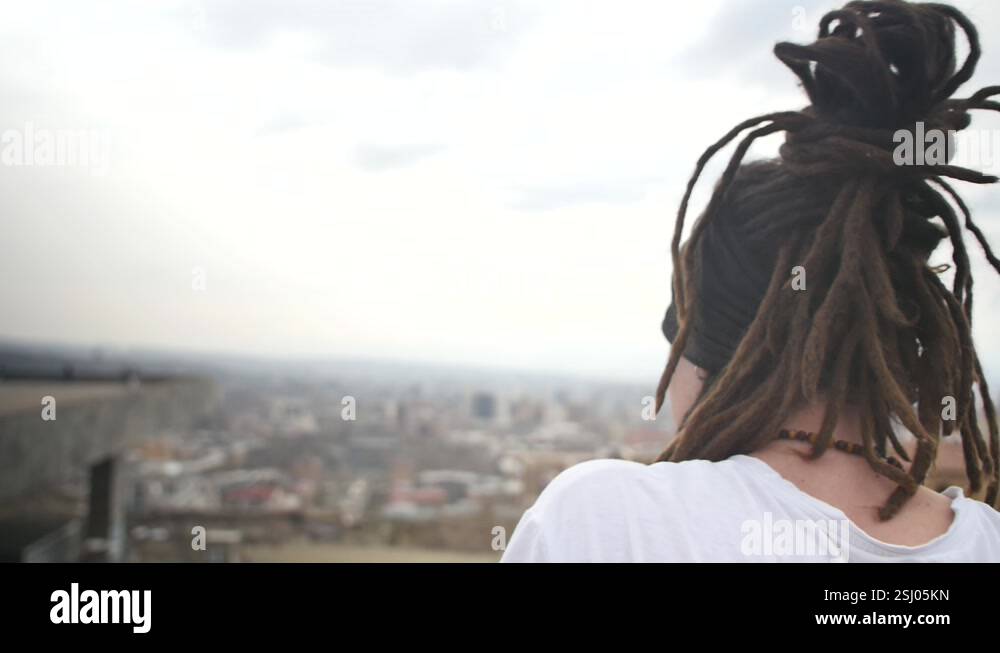 A look from behind a young guy with dreadlocks and beads around his ...