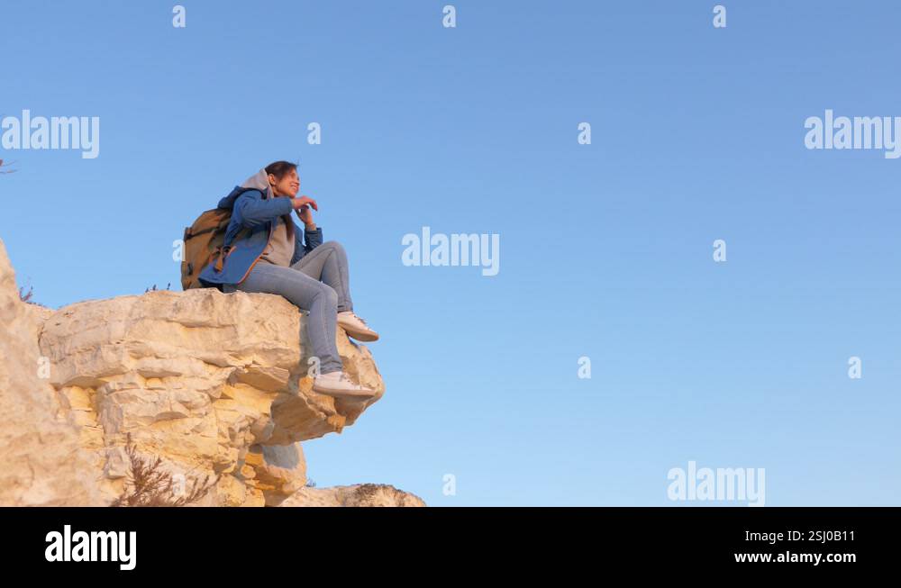 Young woman with tourist backpack, sitting on edge of mountain ...