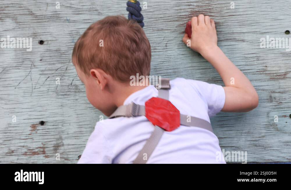 Boy with safety gear climbs up clinging and stepping over ledges on ...