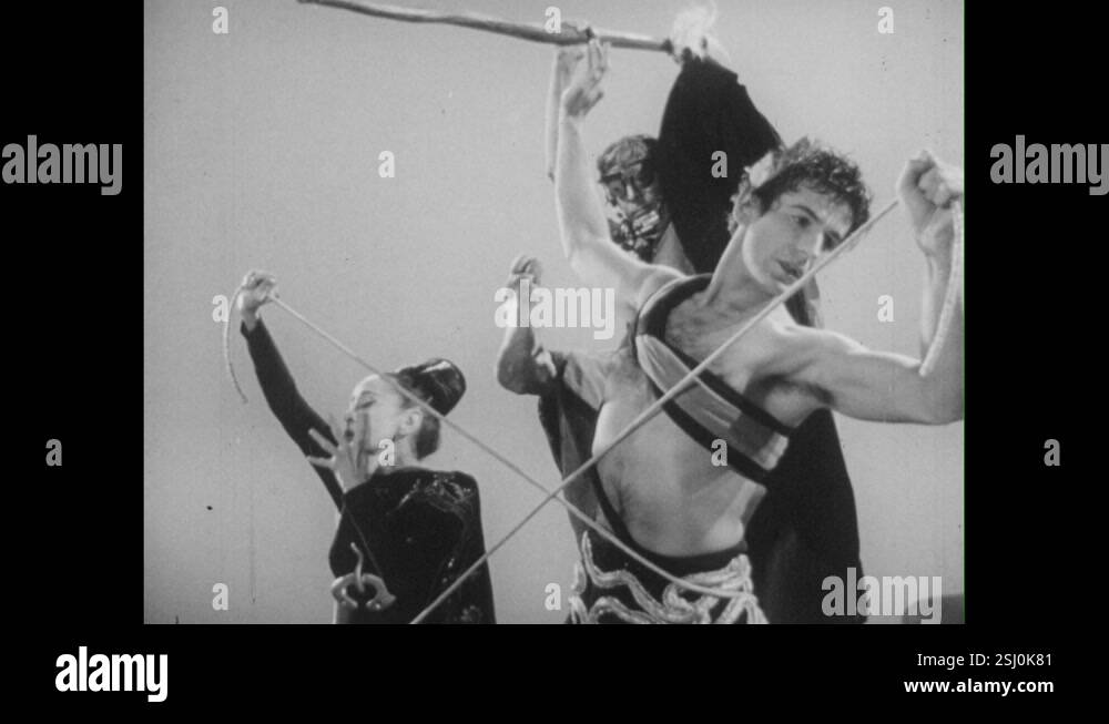 1950s: Couple stand together holding onto rope. Man stands behind them ...