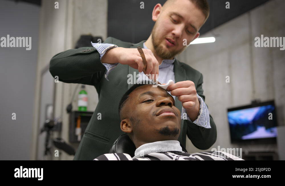 Barber is shaving aligning hair of afroamerican man using razor in ...