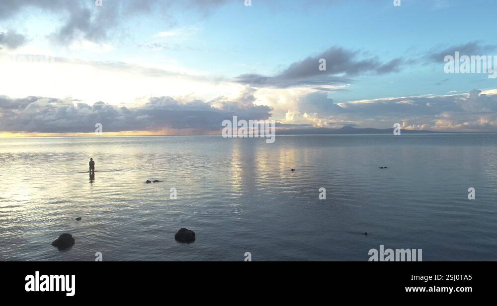 man resting on a sea wall watching another man wading through the water ...