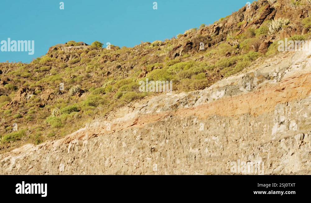 Geological cliff formation with green foliage on top, pan right view ...