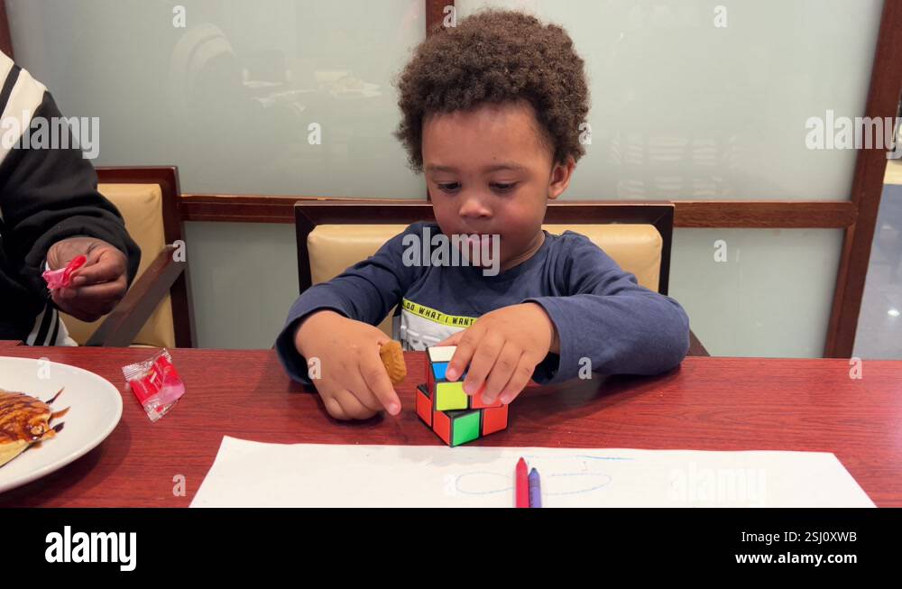 3-year-old black toddler playing with a Rubik’s cube and eating cookies ...