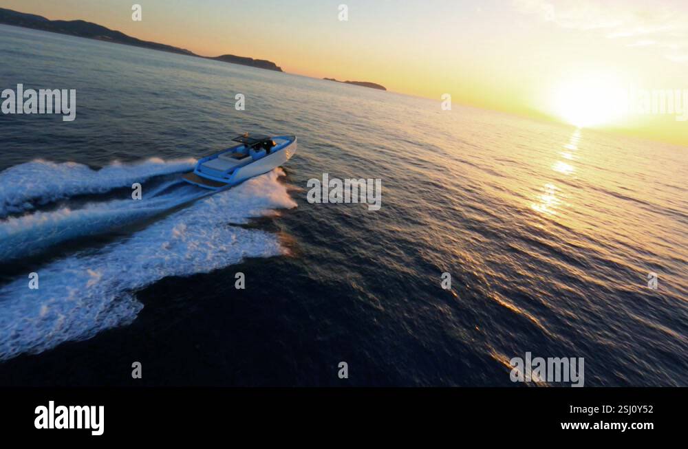 Aerial drone view following a luxury yacht cruising toward the sun as ...