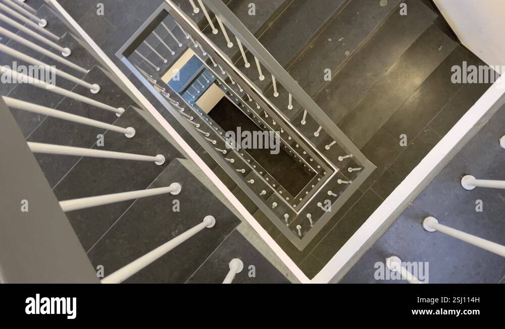 empty stairwell with white railing and dark circled steps behind in a ...