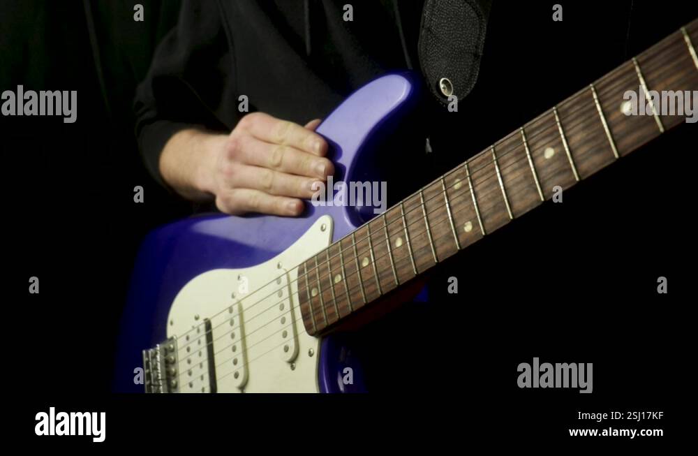 Static shot of a man tapping to the beat on his blue guitar in a studio ...