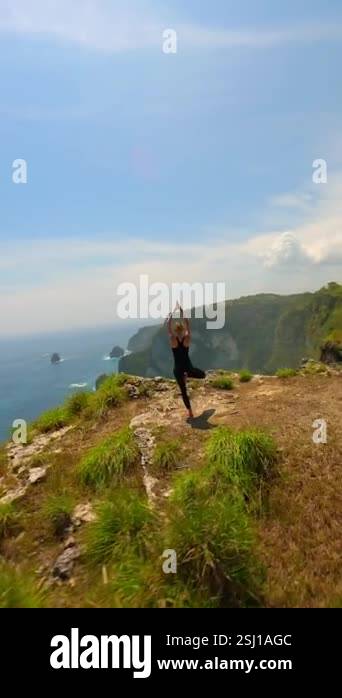 Cinematic FPV shot of athletic woman practicing yoga on a cliff above ...