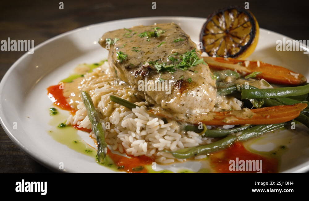 White plate elegantly filled with grilled white fish over pilaf rice ...