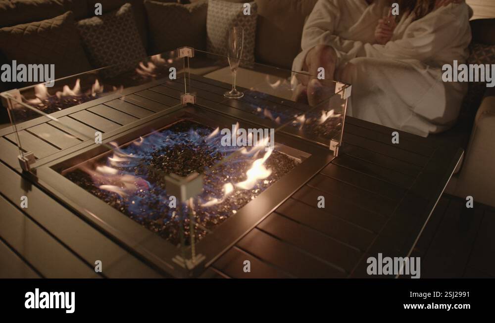 A couple in a romantic relationship sit and relax beside a fire pit at ...