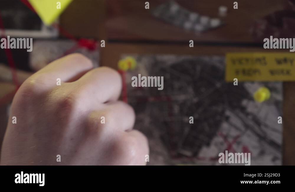 A detective's hand stretches a string between pins on an investigative ...